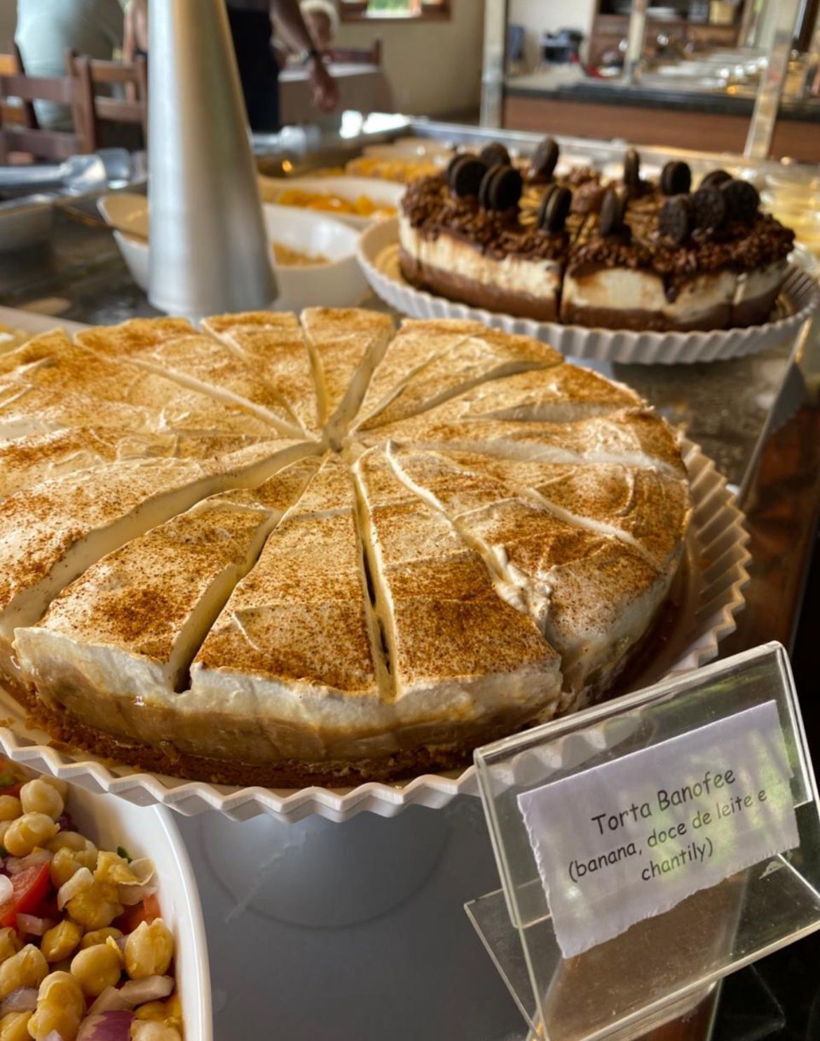 Uma mesa com sobremesas, incluindo uma Tarta Banofee, um doce de banana e creme, e outras opções.
