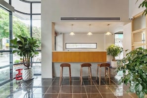 Uma área de recepção com balcão de madeira, três banquetas e plantas em vasos.