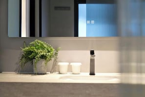 Casa de banho com lavatório, espelho, planta em vaso e duas chávenas brancas.