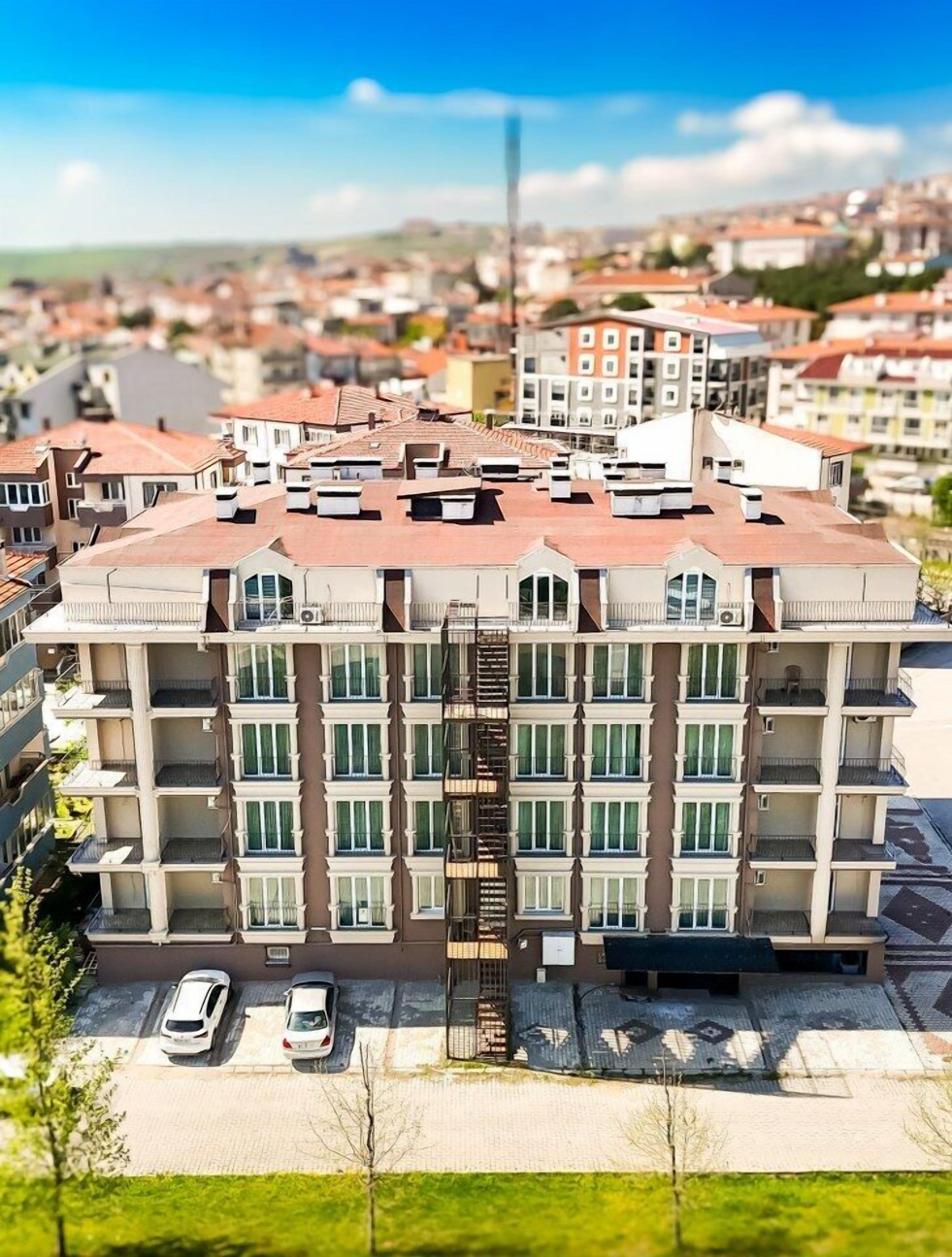 Um edifício com vários andares, uma escadaria central, varandas e um estacionamento com carros.