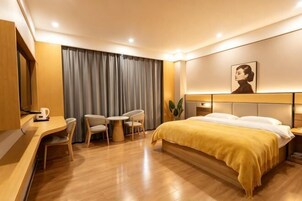 Quarto de hotel com cama, escrivaninha, duas cadeiras, mesa de cabeceira e uma grande janela com cortinas.