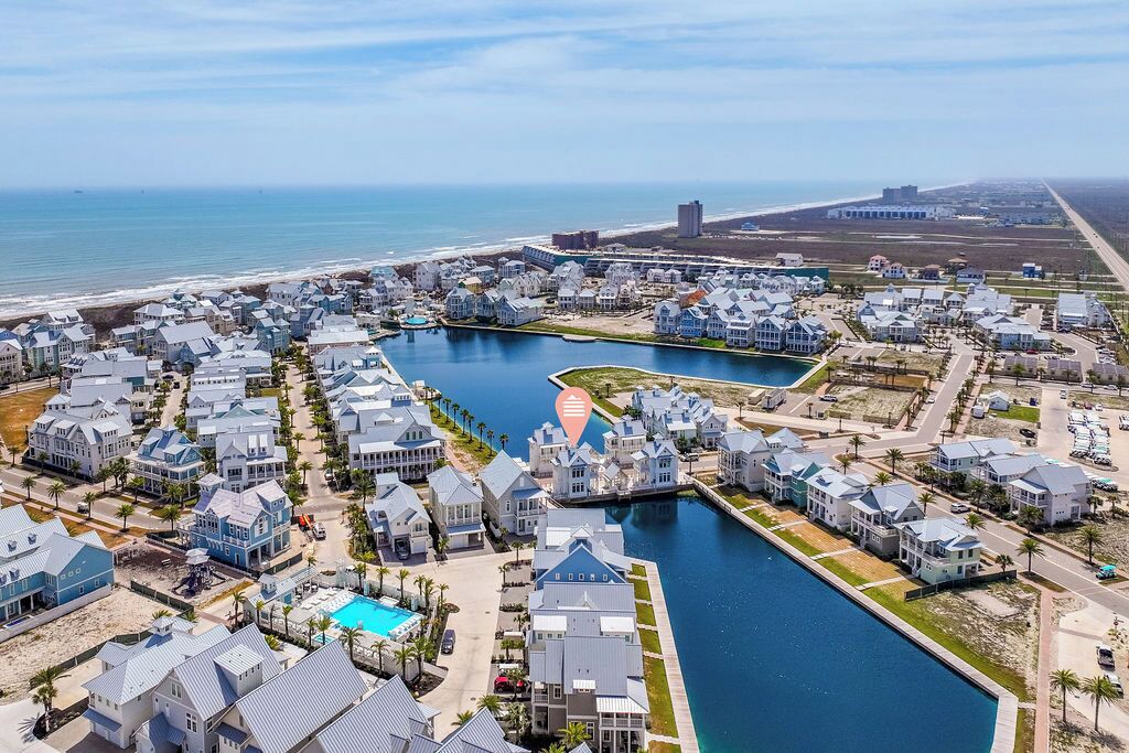 Uma área residencial costeira com casas, um porto de iates e uma praia ao fundo.