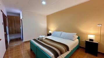 Quarto de hotel com cama, duas mesas de cabeceira com luminárias, guarda-roupa de madeira e chão estampado.