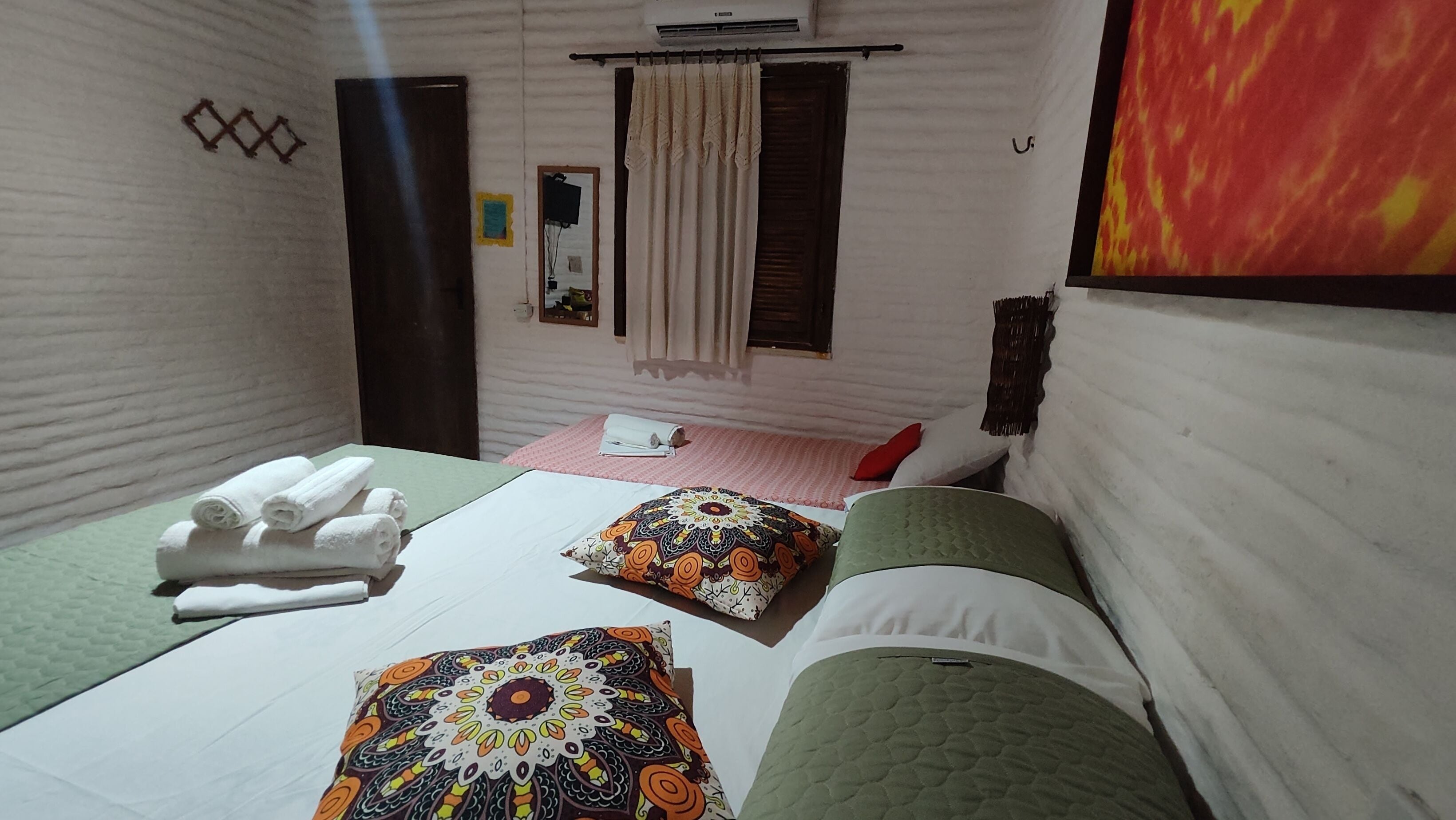 Um quarto pequeno e acolhedor, com duas camas de solteiro, esquema de cores verde e branco, almofada estampada e toalhas dobradas com cuidado.