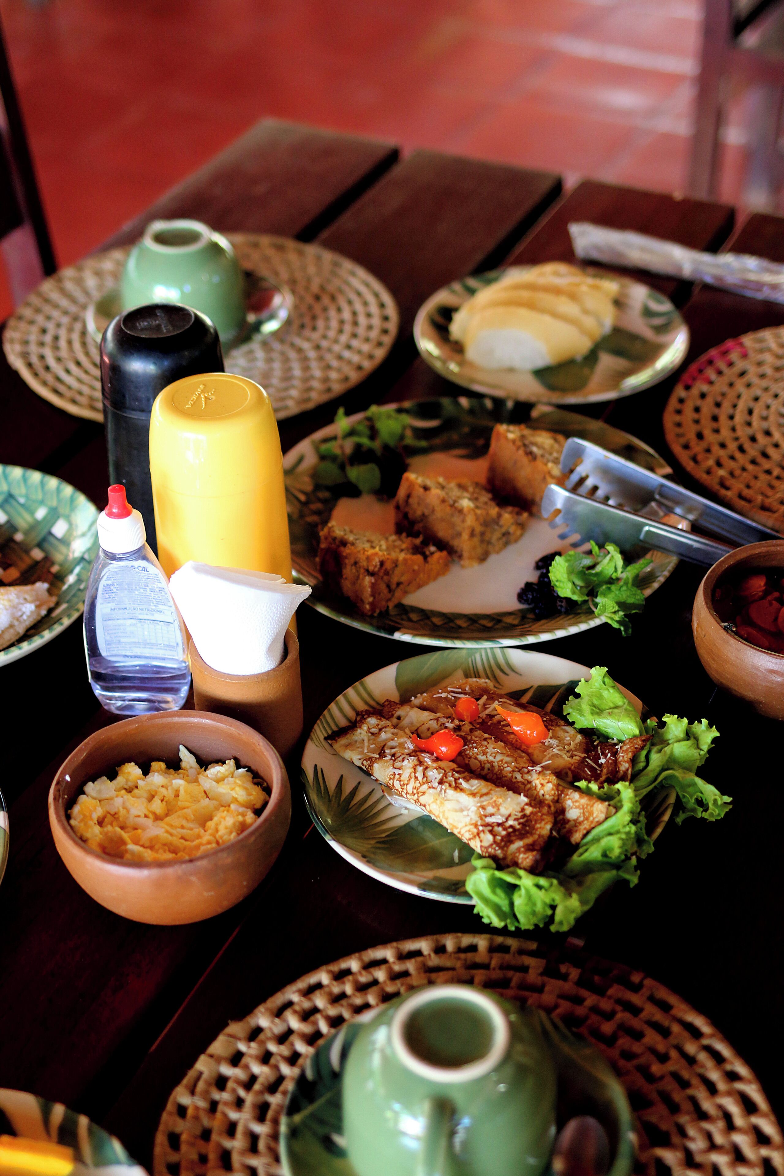 Uma mesa posta com diversos pratos, incluindo uma chaleira verde, uma vela amarela e uma tigela de comida.