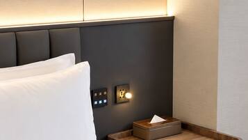 Quarto de hotel com cama, mesa de cabeceira e painel de controle fixado na parede.