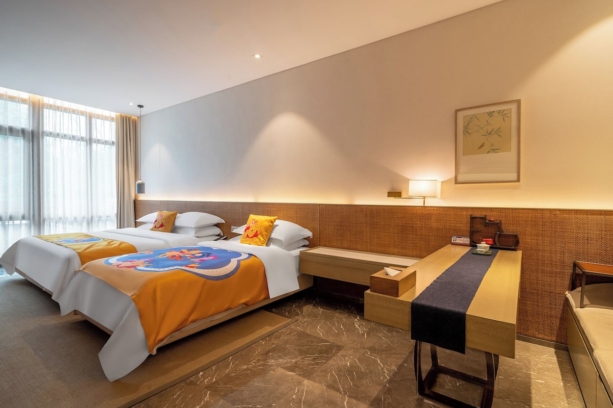 Quarto de hotel com cama, mesa de cabeceira e escrivaninha com cadeira.