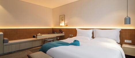 Quarto de hotel moderno com uma cama grande, uma mesa de cabeceira, um banco, uma escrivaninha e um luminário fixado na parede.