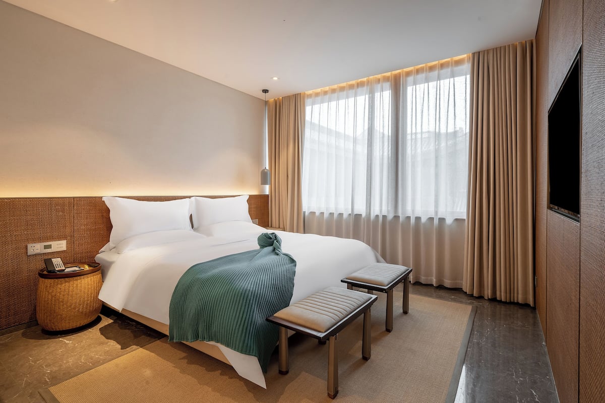 Quarto de hotel com cama grande, mesa de cabeceira e televisão fixada na parede.