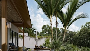 Um pátio moderno ao ar livre com área de estar, pérgola e vista para um jardim exuberante com palmeiras.