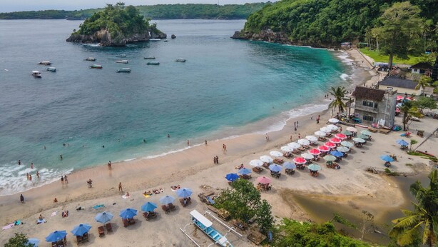 Uma praia com barcos, guarda-sóis e pessoas.