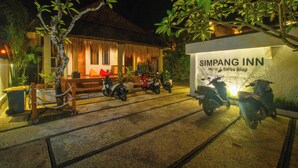 Um edifício com uma placa indicando "SIMPANG INN" e uma cafeteria. Várias motocicletas estão estacionadas em frente.