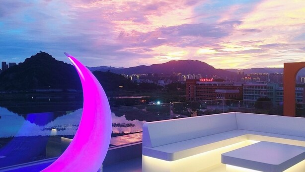 Terraço no telhado com mobiliário moderno e uma grande escultura em forma de crescente iluminada.
