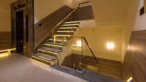 Uma escadaria moderna com guarda-corpos de vidro e iluminação embutida, que leva a um patamar no segundo andar.
