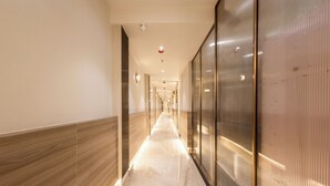Corredor com painéis de madeira à esquerda, parede de vidro à direita e piso de mármore.
