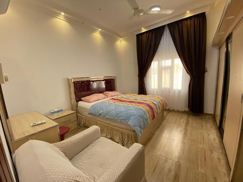 Quarto de hotel com cama, mesa de cabeceira, cadeira e ventoinha no teto.