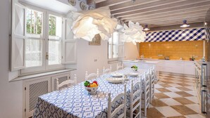 Uma sala de jantar com uma mesa posta para quatro pessoas, uma cozinha ao fundo e uma luminária decorativa no teto.