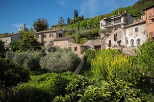 Uma aldeia numa encosta com edifícios de pedra, vegetação exuberante e céu azul límpido.