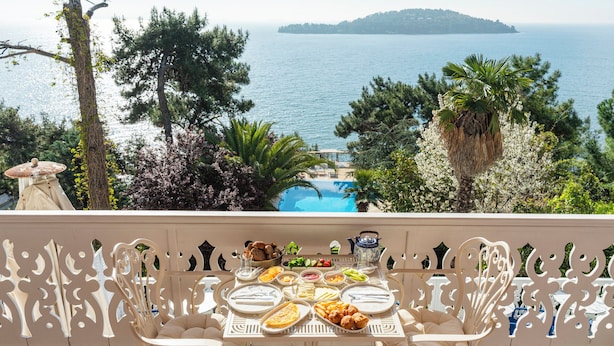 Varanda com mesa posta para refeição, vista para uma piscina e o mar.