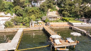 Um cais com espreguiçadeiras e guarda-sóis, um barco pequeno e um edifício de pedra com um jardim.