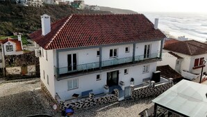 Um edifício de dois andares com telhado em telhas, varanda e vista para o mar.