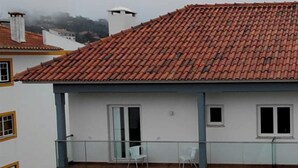 Um edifício com telhado de telhas vermelhas, paredes brancas e uma varanda com duas cadeiras.