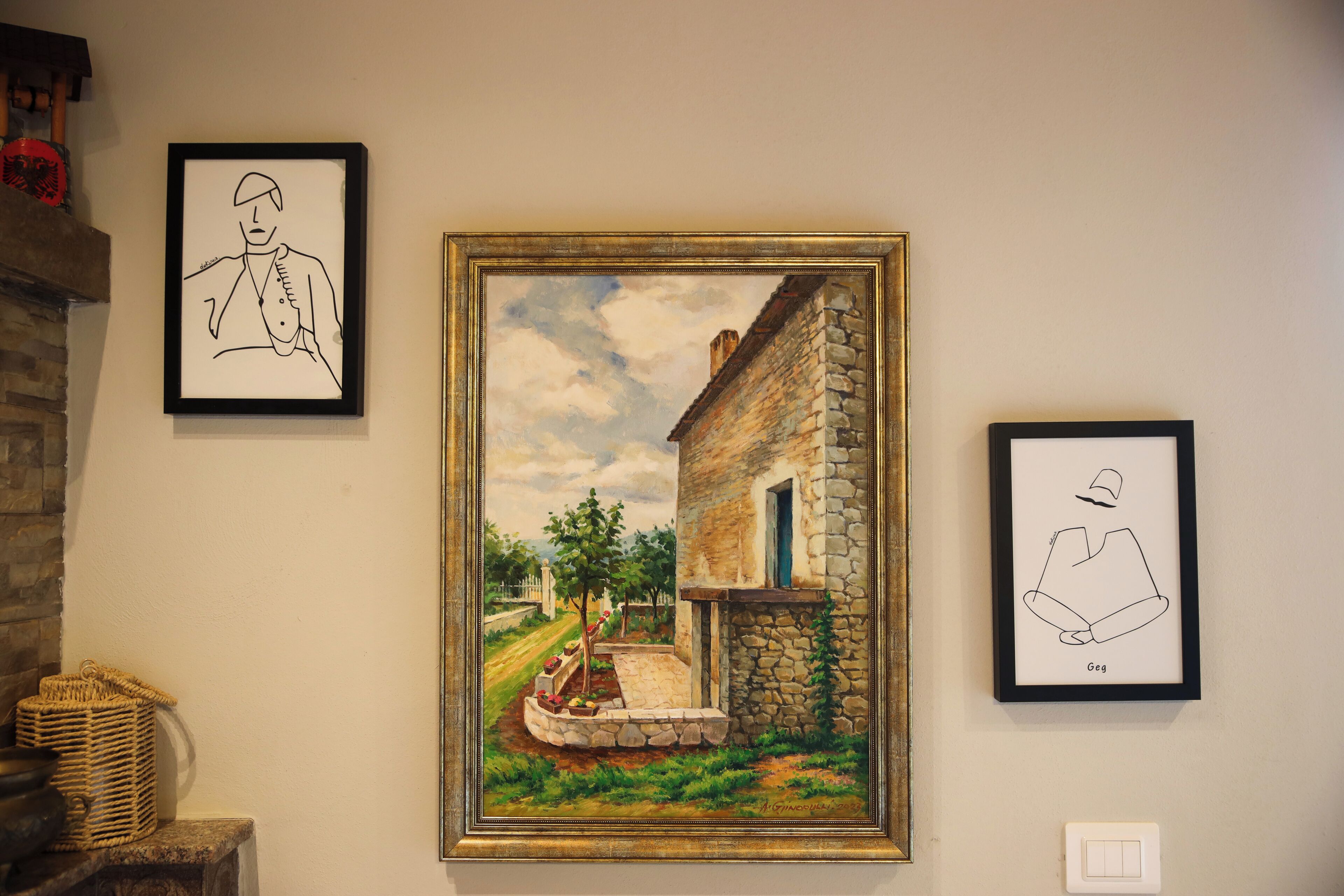Um quadro emoldurado de um edifício de pedra com um caminho e árvores, e dois desenhos menores na parede.