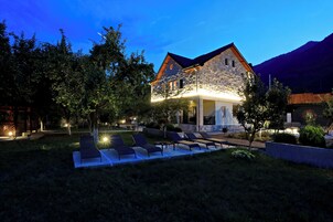 Uma casa de pedra com telhado inclinado, piscina com espreguiçadeiras e área de jardim bem iluminada.