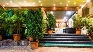 Entrada de hotel com degraus que levam a uma porta, cercada por plantas em vasos.