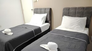 Duas camas de solteiro com cabeceiras cinzas e roupa de cama branca, cada uma com uma toalha branca e um cobertor cinza.