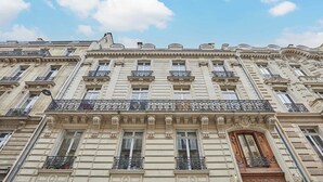 Um edifício com vários andares e detalhes arquitetônicos requintados, incluindo varandas decorativas e uma porta de madeira imponente.