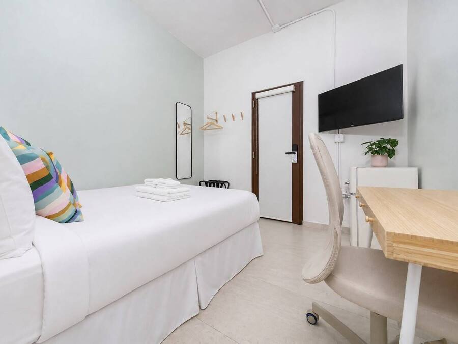 Quarto de hotel com cama, escrivaninha, cadeira, televisão e porta.