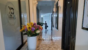 Um corredor com um vaso branco cheio de flores coloridas, uma parede de vidro com um logotipo e piso de mármore.