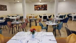 Um restaurante com várias mesas, cada uma posta com toalhas brancas, copos e talheres.