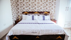 Uma cama com colcha branca e confortável, cabeceira de madeira e piso de mármore.