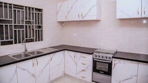 Cozinha com armários de mármore branco, bancada preta, fogão de aço inoxidável e janela com grades de metal.