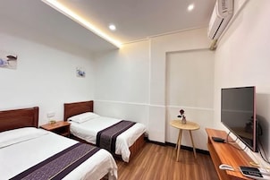 Quarto de hotel com duas camas, uma mesinha redonda, televisão e escrivaninha de madeira.