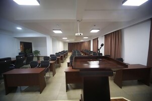 Uma sala de conferências com mesas e cadeiras compridas, um projetor e uma tela grande.