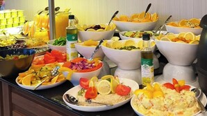 Buffet com diversos pratos, incluindo saladas, frutas e um prato quente.