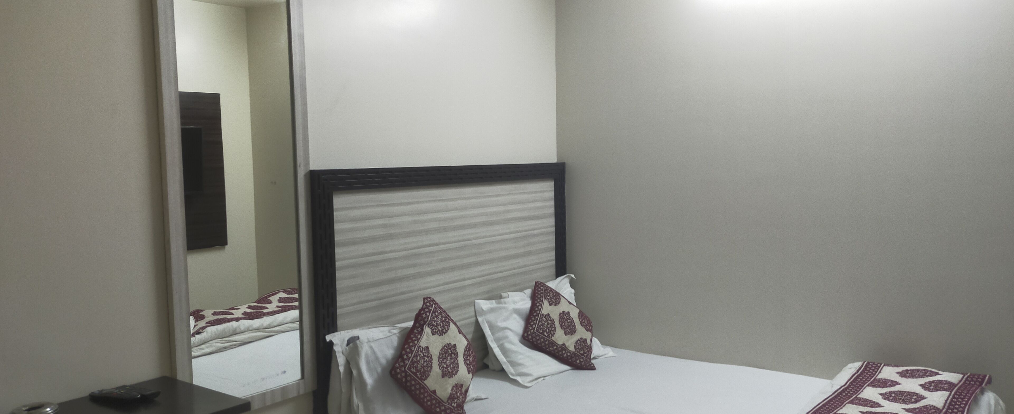 Quarto de hotel com cama, mesa de cabeceira, espelho e luminária na parede.
