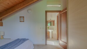 Quarto com cama, luminária de cabeceira, quadro na parede e ar-condicionado.