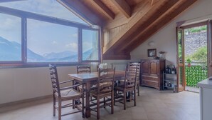 Uma área de refeições com mesa e cadeiras de madeira, janelas amplas com vista para as montanhas e um espaço de cozinha com armários e uma planta.