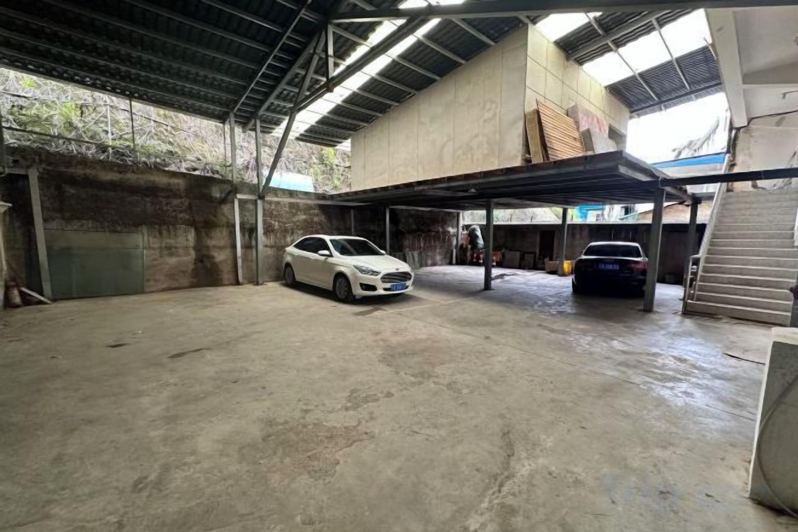 Uma área de estacionamento coberta com dois carros estacionados sob um telhado, piso de concreto e teto metálico.
