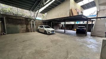 Uma área de estacionamento coberta com dois carros estacionados sob um telhado, piso de concreto e teto metálico.