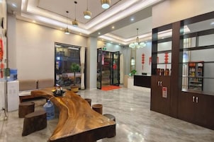 Um saguão de hotel com balcão de recepção, área de estar e uma grande mesa de centro de madeira.