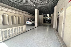 Corredor com um carro branco estacionado, piso de azulejos e teto com padrão quadriculado.
