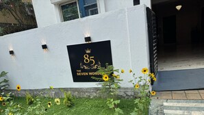 Um edifício com uma placa que diz "85 The Seven Wonders" e um jardim com girassóis.