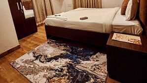 Quarto de hotel com uma cama, televisão, guarda-roupa e um tapete grande.