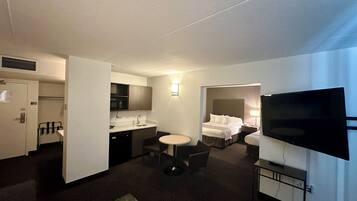 Quarto de hotel com cama, televisão, pequena mesa de jantar, cozinha e banheiro.