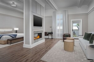 Quarto de hotel moderno com cama grande, lareira, televisão de tela plana, sofá e área de jantar.